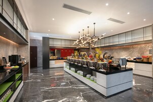 Um hall de hotel moderno com área de buffet, piso de mármore e luminárias contemporâneas.
