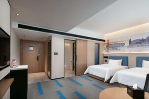 Quarto de hotel com duas camas, uma mesa com uma garrafa de água, televisão e porta do banheiro.