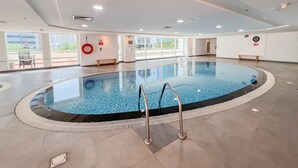 Piscina interior com paredes de vidro transparente, um flutuador e um banco.
