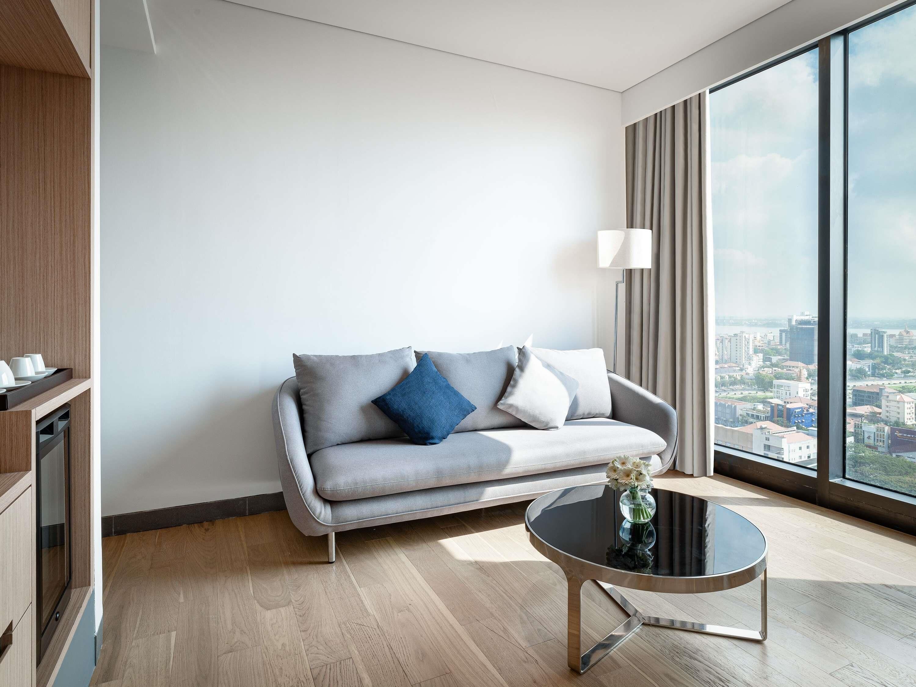 Uma sala de estar moderna com um sofá, uma mesa de centro de vidro e vista para o horizonte urbano por grandes janelas.