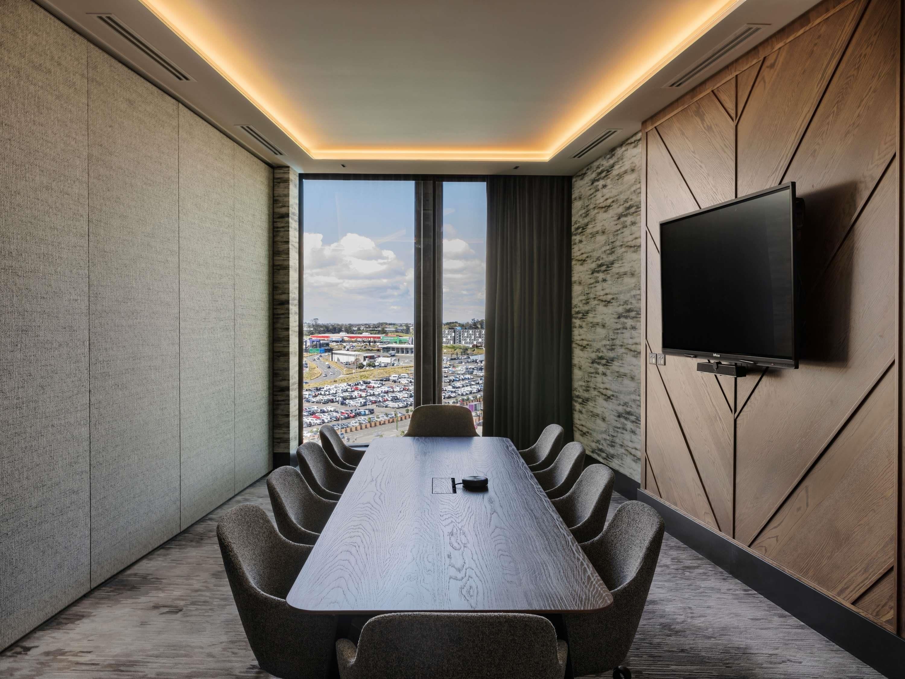 Uma sala de conferências com uma mesa comprida, cadeiras, uma televisão e vista para um horizonte urbano através de grandes janelas.