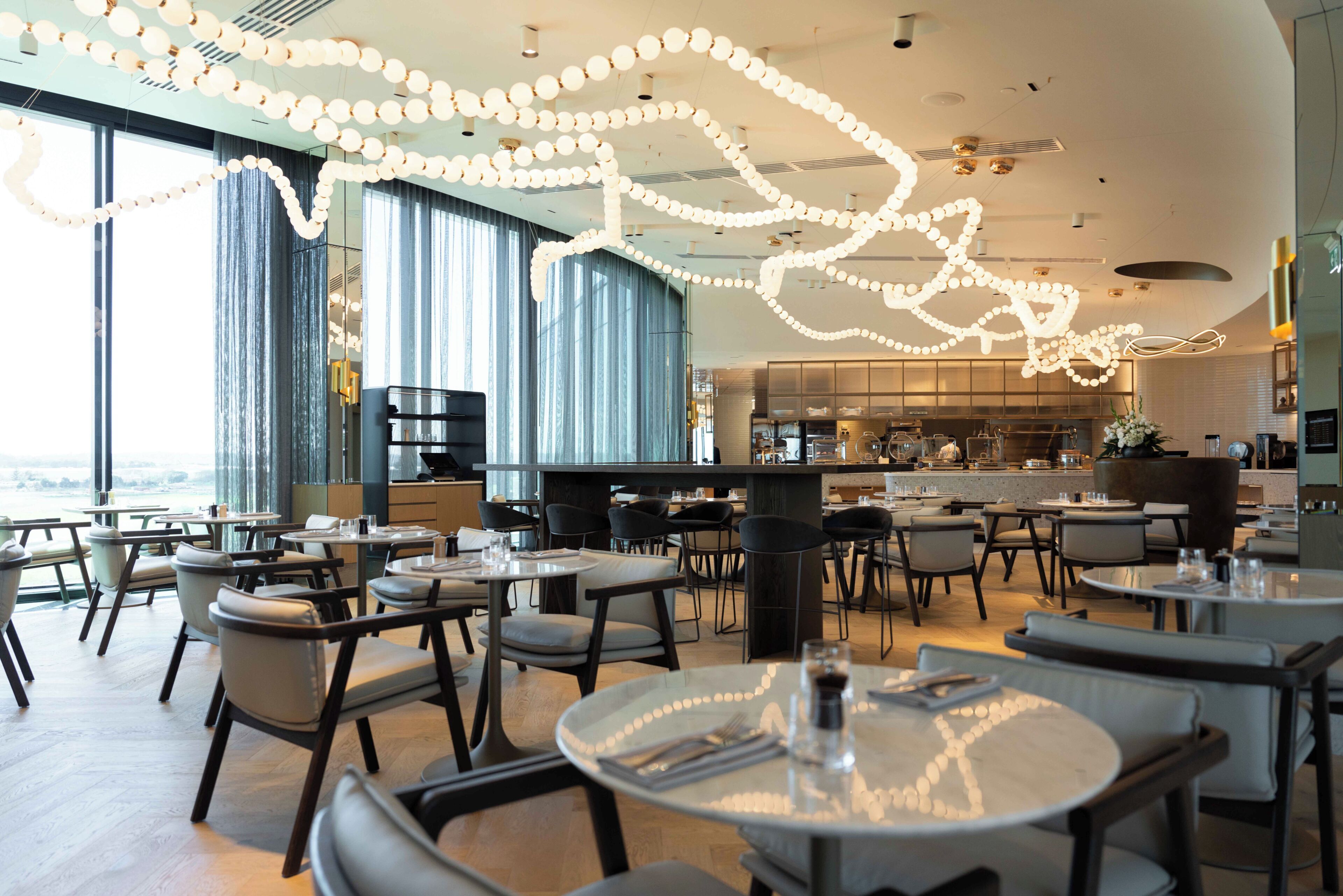 Um restaurante moderno com mesas redondas, cadeiras e um espaço de bar.