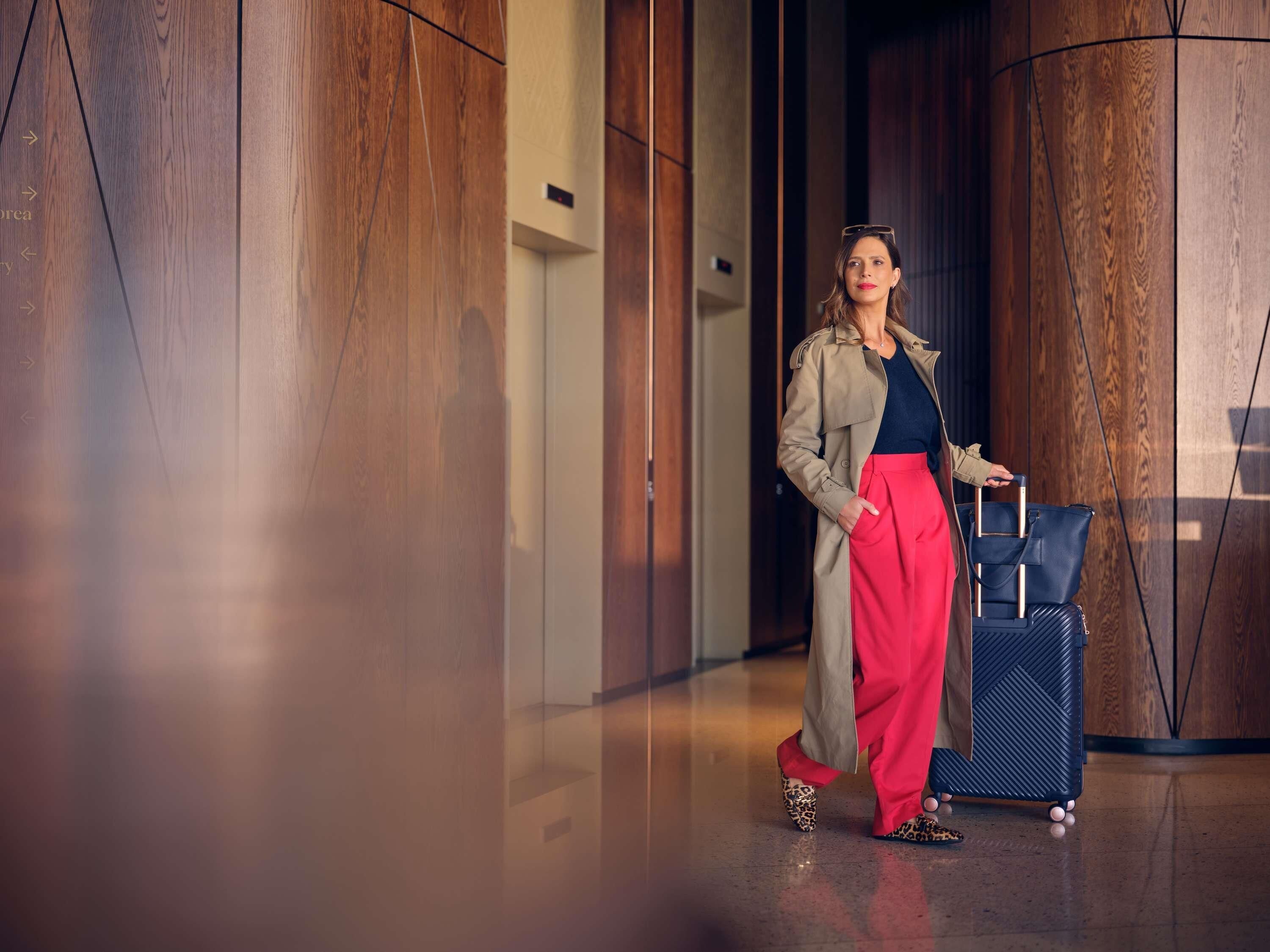 Uma pessoa em um corredor com mala e bolsa, paredes de madeira e design moderno.