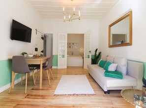 Uma sala de estar moderna com área de jantar, um sofá com almofadas verdes, uma televisão de tela plana e um lustre.