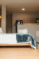 Quarto com cama, mesa de cabeceira e pequena área de cozinha equipada com micro-ondas e cafeteira.