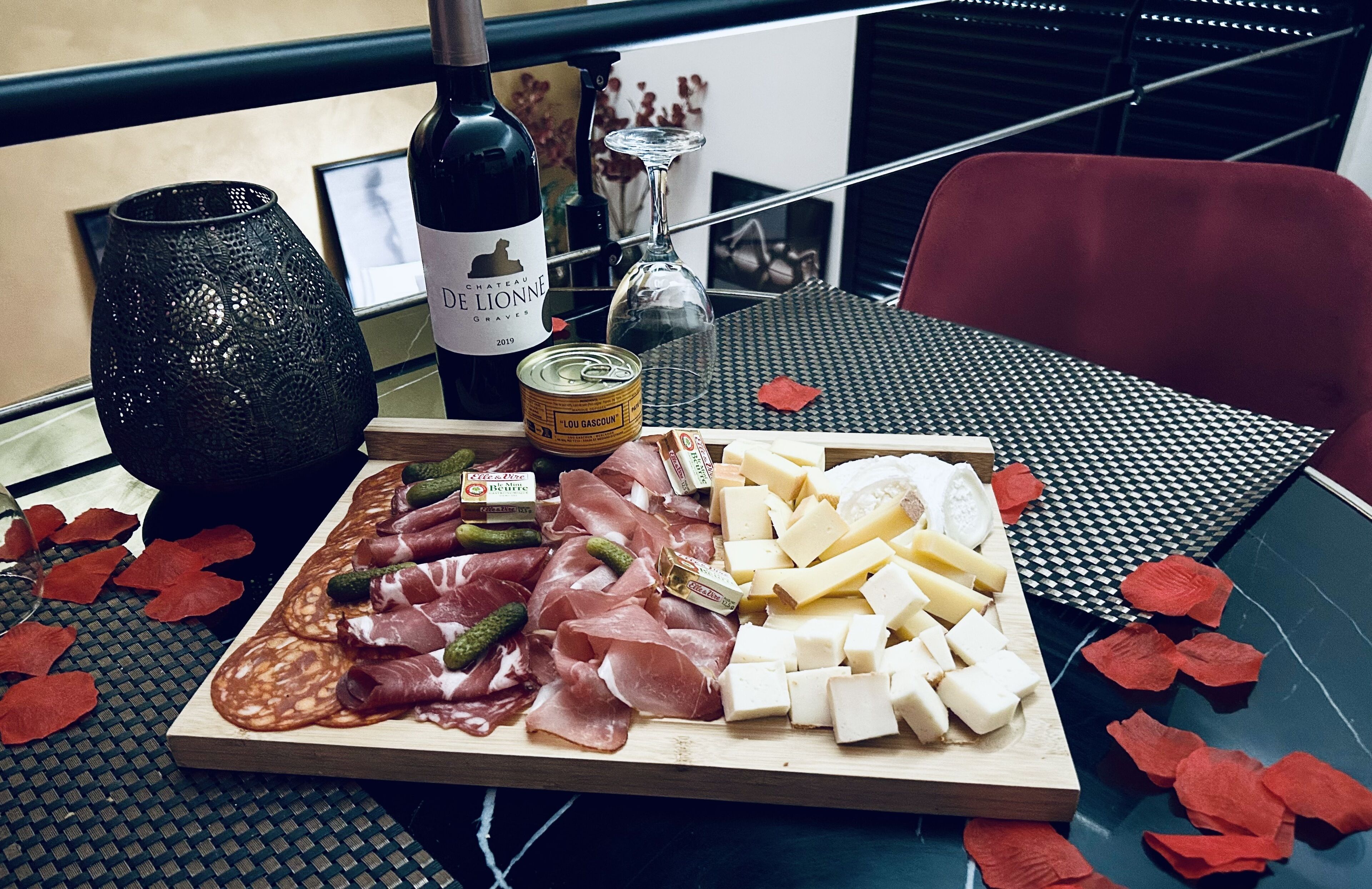 Uma tábua de frios com diversos queijos, carnes e uma garrafa de vinho sobre uma mesa.
