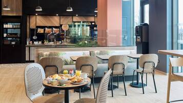 Um café moderno com mesas e cadeiras redondas, um balcão com um chef e vista para a cidade.