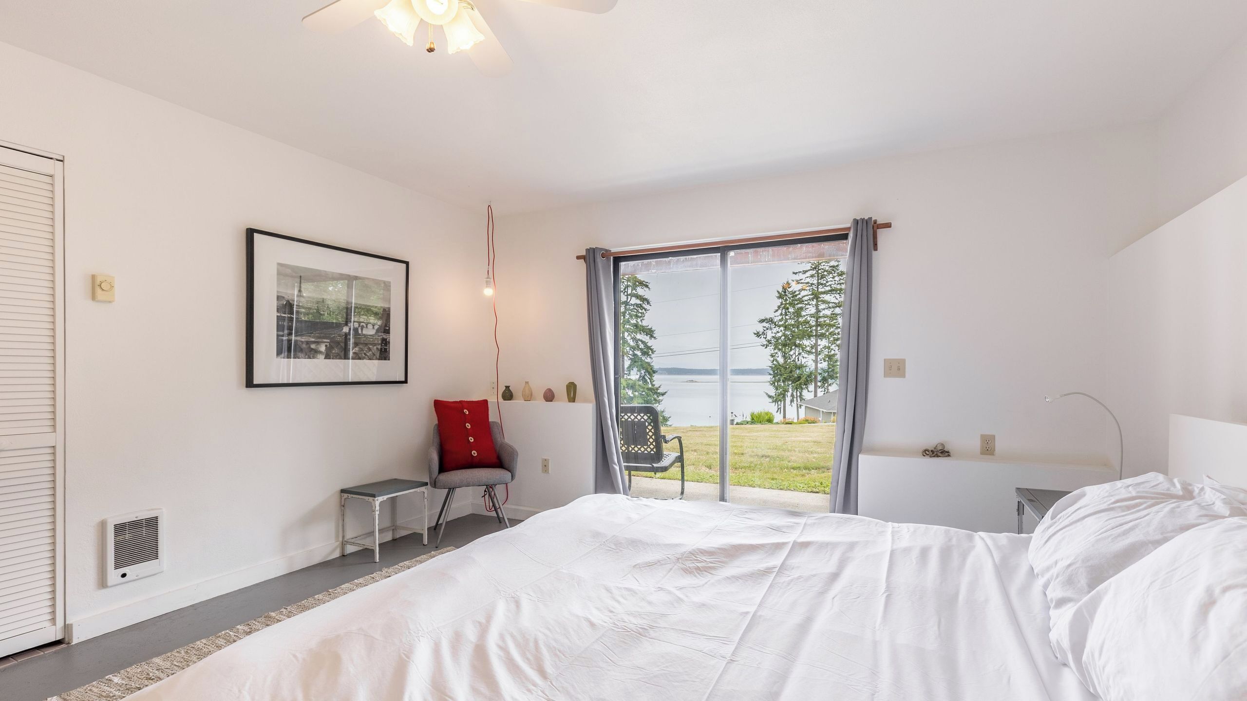 Quarto com cama, cadeira, escrivaninha, janela com vista para o exterior e luminária no teto.