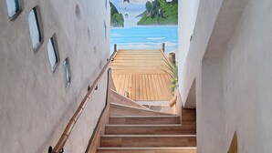 Uma escadaria de madeira leva a uma vista da praia, com um mural de paisagem tropical na parede.