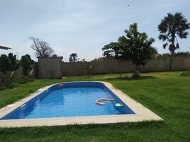 Piscina retangular com interior azul, rodeada por um deck de concreto e uma área gramada.