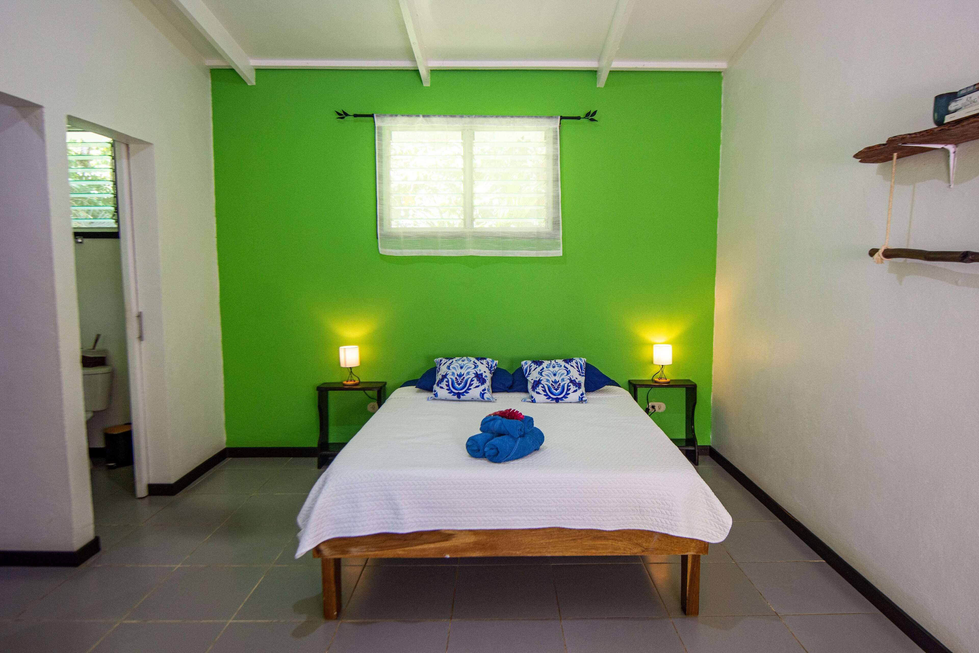 Um quarto com uma cama, duas luminárias de cabeceira, uma janela com cortina e uma parede verde.
