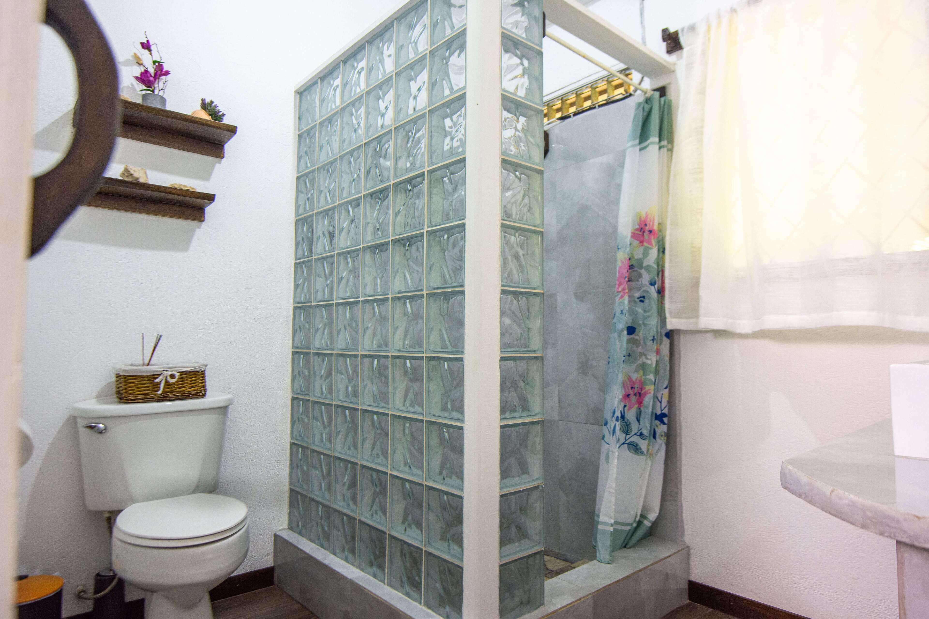 Casa de banho com cabine de chuveiro em vidro, sanita e lavatório com bancada de mármore.