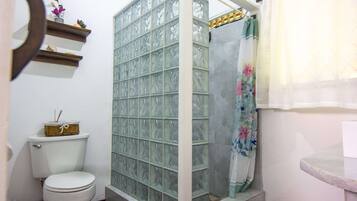 Casa de banho com cabine de chuveiro em vidro, sanita e lavatório com bancada de mármore.