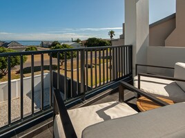 Uma varanda com vista para o mar, uma palmeira e uma rua com casas.