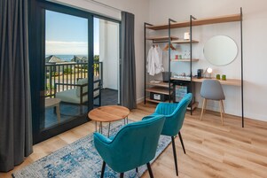 Quarto moderno com varanda, uma escrivaninha com cadeira, espelho redondo e prateleira com roupas e artigos de higiene.