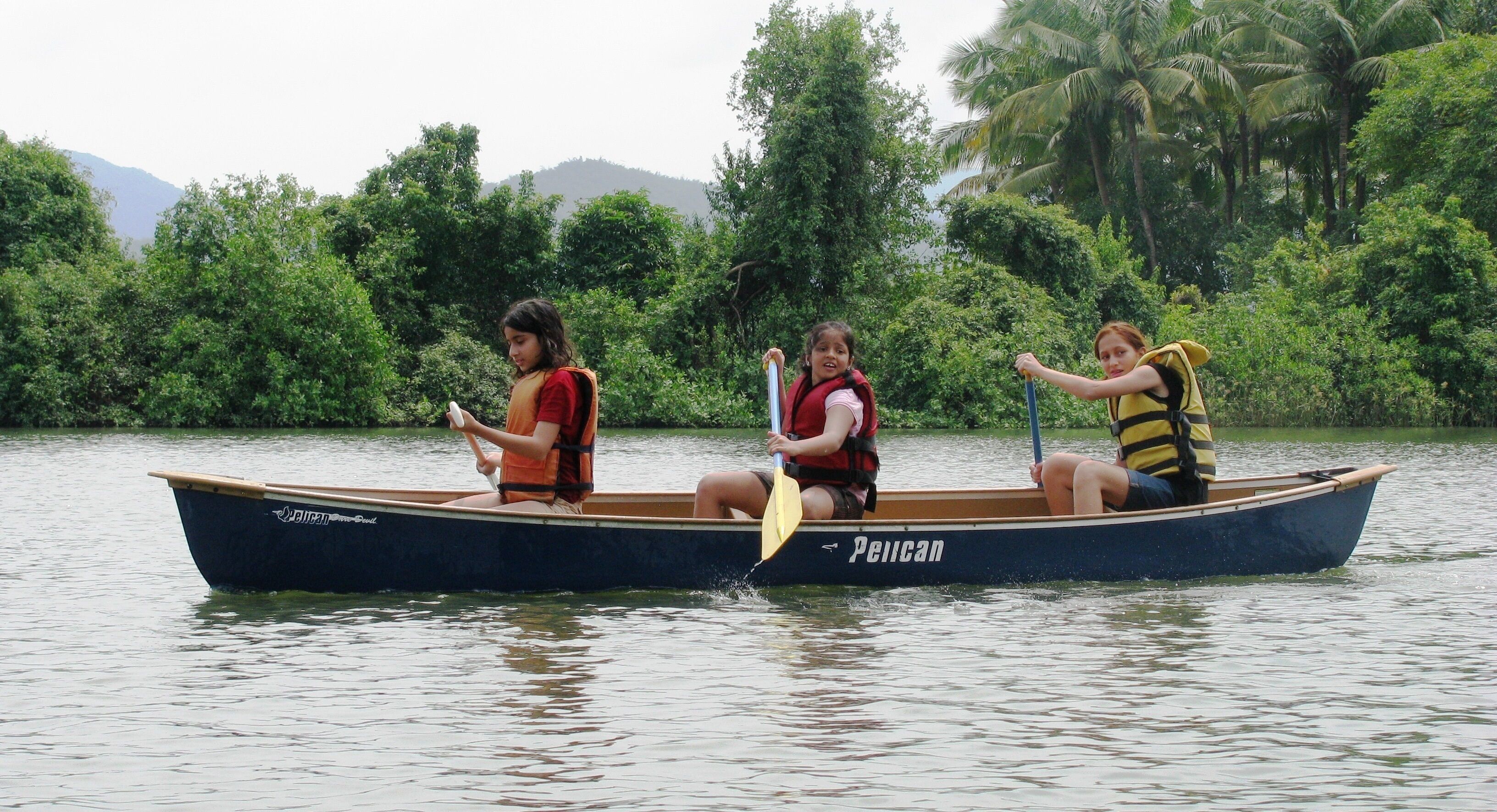 Três pessoas em um barco num rio calmo, rodeadas por vegetação exuberante.