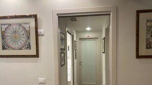 Um corredor com quadros nas paredes, uma porta no final e um interruptor de luz na parede.