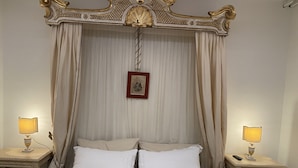 Quarto com cama de dossel, duas mesinhas de cabeceira com luminárias e um quadro pendurado na parede.