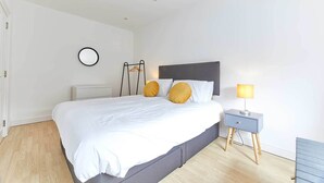 Quarto moderno com cama, mesa de cabeceira e espelho fixado na parede.