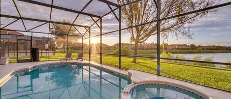 Piscina com vista para um pôr do sol e uma área gramada ao fundo.