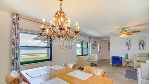 Um quarto amplo com uma mesa de jantar de madeira, assentos confortáveis, um candelabro e vista para o exterior.