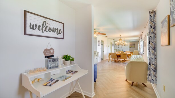 Um interior moderno com um console branco exibindo uma placa de boas-vindas, um letreiro com a frase 'Seja Nosso Convidado' e uma placa com a inscrição 'Lago das Memórias'.