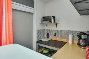 Uma cozinha compacta com micro-ondas em uma prateleira, cafeteira e chaleira na bancada.