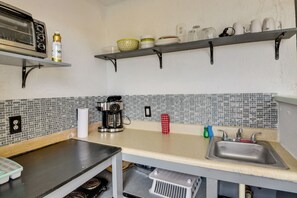 Cozinha equipada com micro-ondas, cafeteira e pia. Há prateleiras sobre o balcão com louças e uma garrafa.