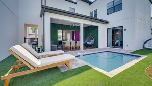 Uma casa moderna com piscina, um pátio com cadeiras de descanso e uma área de refeições com mesa e cadeiras.