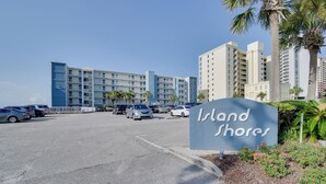 Placa de hotel com a inscrição 'Island Shores', cercada por um estacionamento com vários carros e palmeiras.
