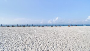 Uma extensa praia de areia com fileiras de cadeiras e guarda-sóis azuis.