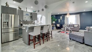 Cozinha moderna com área de bar, espaço de refeições com banquetas e sala de estar com sofá e apoio para os pés.