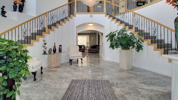 Um hall espaçoso com uma escadaria imponente, piso de mármore e vasos decorativos.