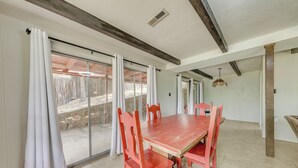 Uma área de refeições com uma mesa grande e cadeiras, uma porta de vidro deslizante e um teto com vigas aparentes.