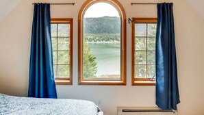 Quarto com cama grande, janela com cortinas e vista para um lago e floresta.