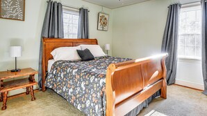 Quarto com cama de madeira, mesa de cabeceira, ventilador de teto e janela com cortinas.