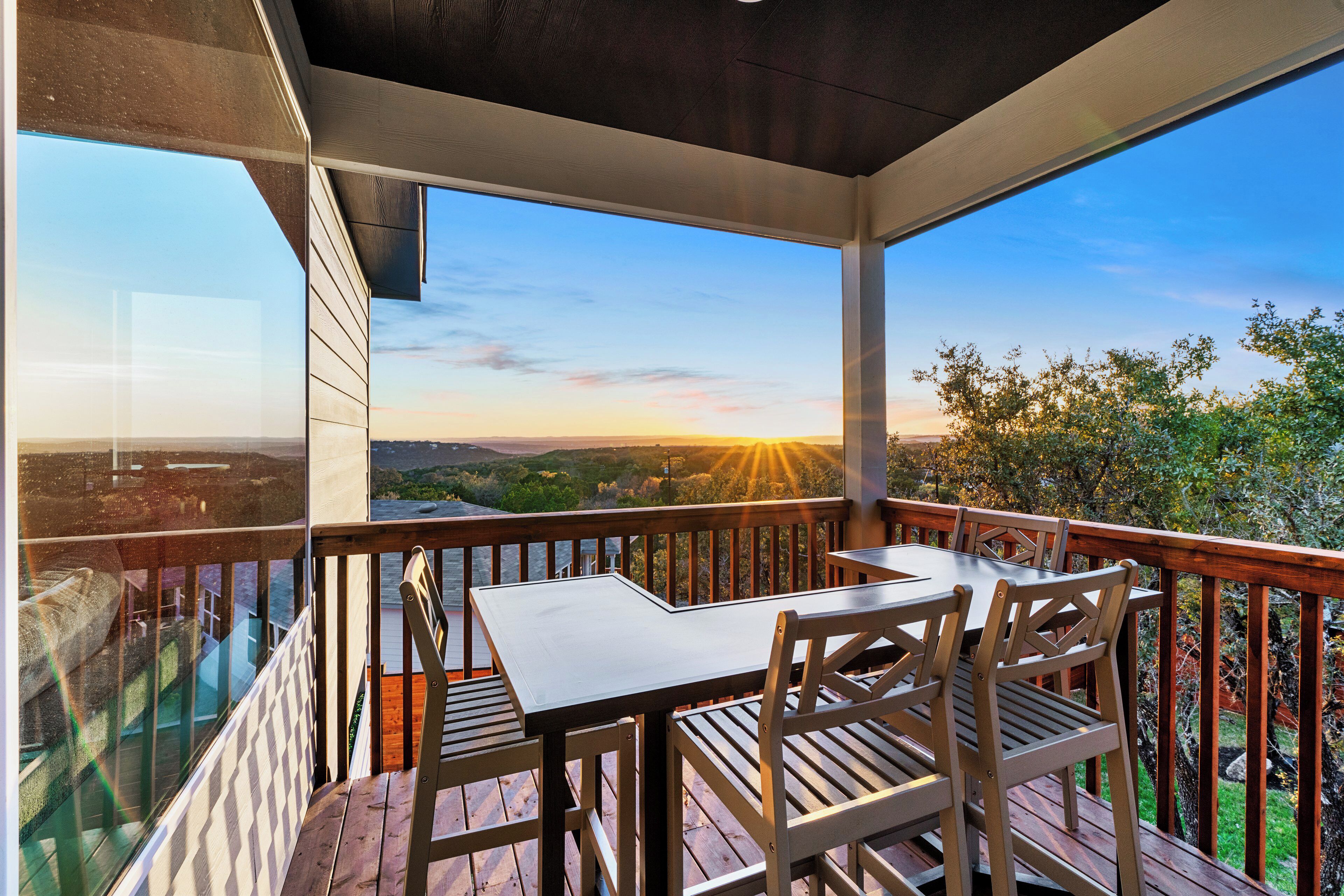 Um deck de madeira com mesa e cadeiras, com vista para uma paisagem deslumbrante ao pôr do sol.