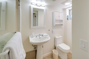 Casa de banho com lavatório branco, espelho e sanita. Há um porta-toalhas e um pequeno armário sobre o lavatório.
