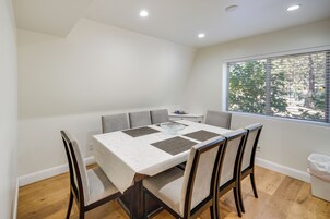 Uma área de refeições com uma mesa retangular, seis cadeiras e uma janela com persianas.