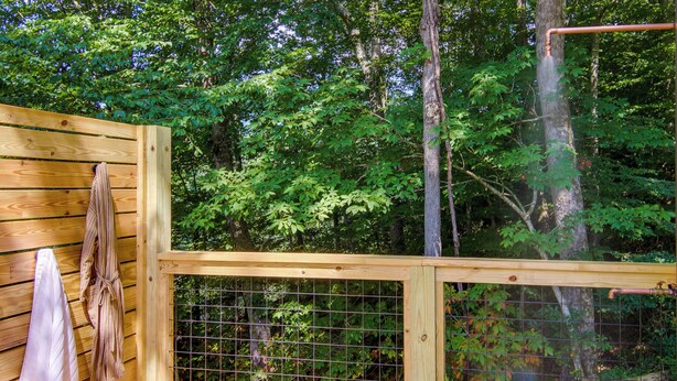 Um deck de madeira com guarda-corpo de metal, uma toalha pendurada na parede e vista para uma área arborizada.