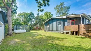Uma casa pequena e térrea com um quintal cercado, um deck de madeira e uma porta vermelha.