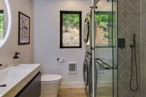 Uma casa de banho moderna com um espelho grande, uma sanita, uma máquina de lavar roupa e uma janela com vista para vegetação.