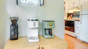 Cozinha com cafeteira, um coador de café manual e moedor de café em uma bancada de madeira.