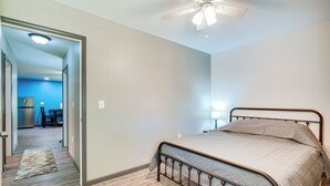Quarto com cama, ventilador de teto e corredor visível que dá para uma área de cozinha.