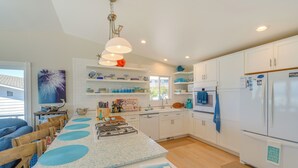 Uma cozinha moderna com armários brancos, uma ilha central com detalhes em azul, forno embutido e geladeira com ímãs.
