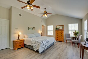 Quarto com cama, mesas de cabeceira de madeira, cômoda, cadeira, escrivaninha e ventilador de teto.