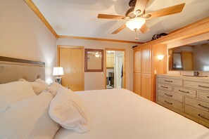 Quarto com cama, cabeceira de madeira, ventilador de teto, cômoda e espelho.