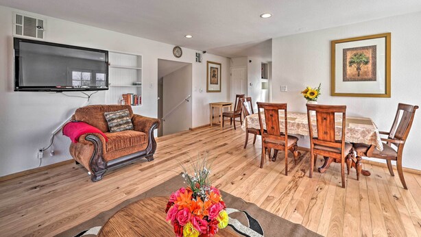 Uma sala de estar com sofá, uma mesa de jantar com cadeiras, uma TV fixada na parede e um quadro pendurado na parede.