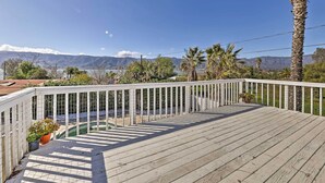 Um deck de madeira com guarda-corpo branco, plantas em vasos e vista para montanhas e um corpo d'água.