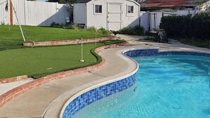 Uma piscina com azulejos de mosaico azul, borda de tijolos e gramado.